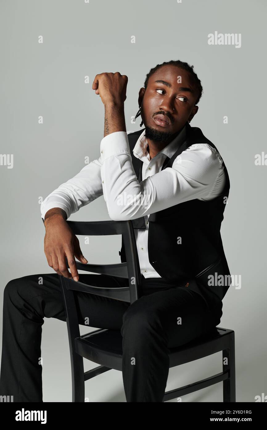 A young man dressed in a sharp suit and vest poses with poise on a grey ...