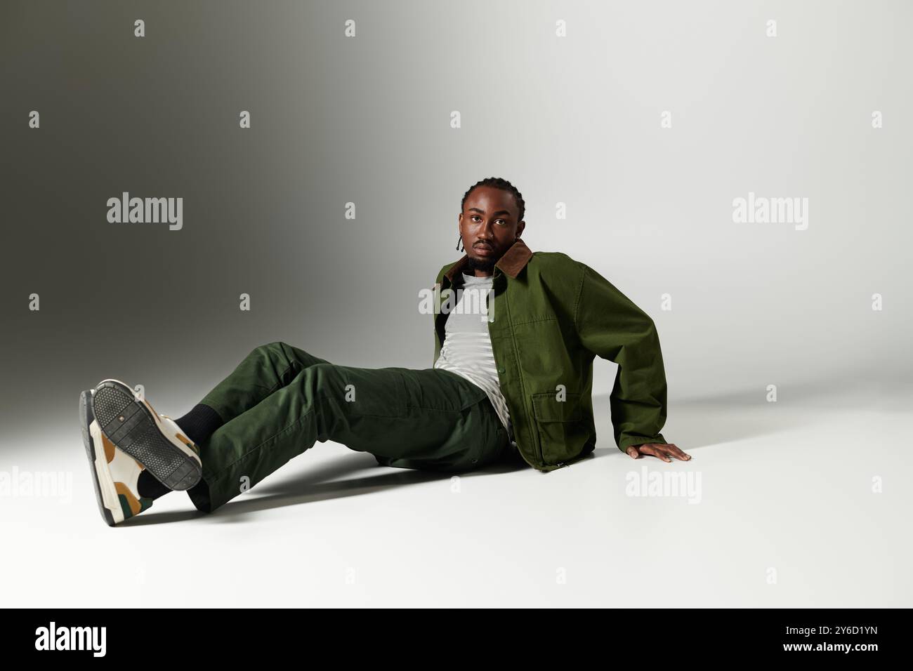 A young man dressed in a chic green outfit sits on the floor with a ...