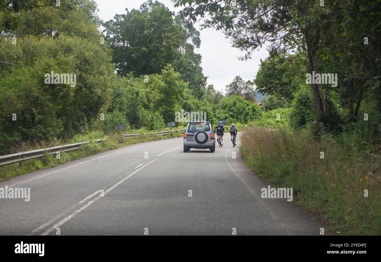 All-terrain vehicle moving slowly behind two cyclists placed side by ...