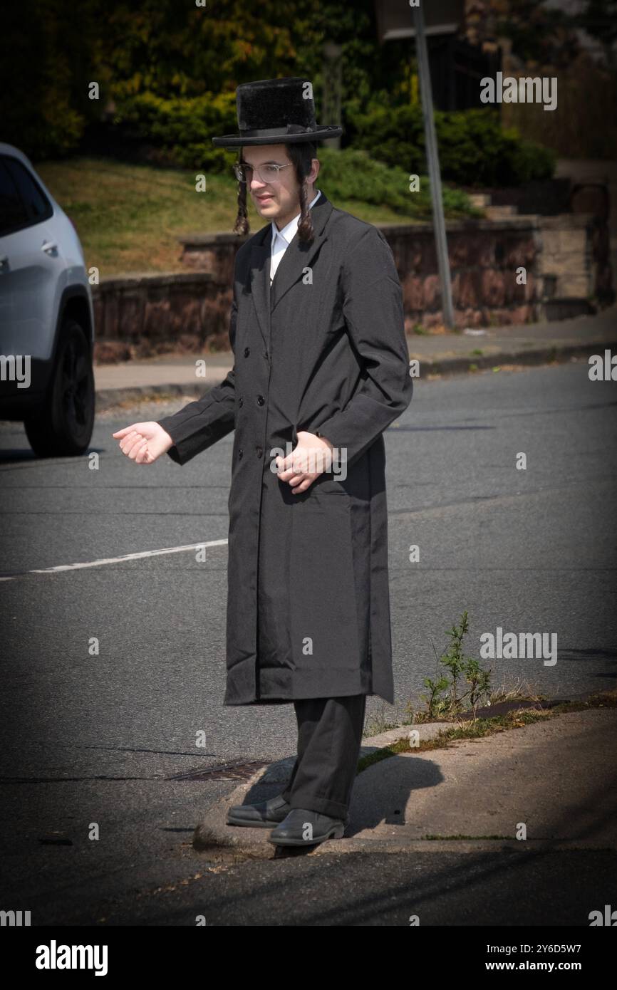 An orthodox young man with long curly peyus sticks his thumb out to ...