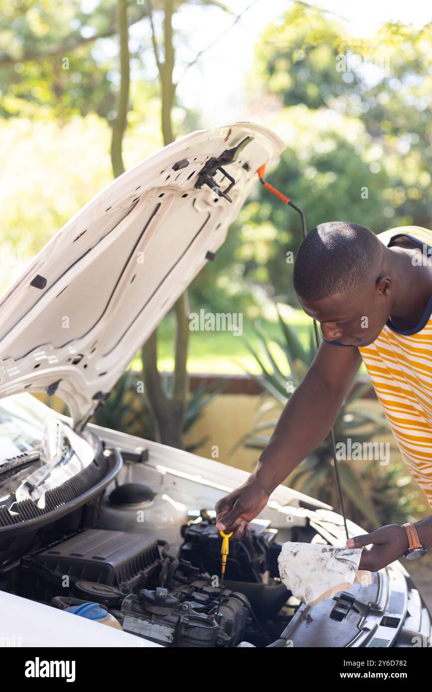 Checking car engine oil, african american man in striped shirt ...