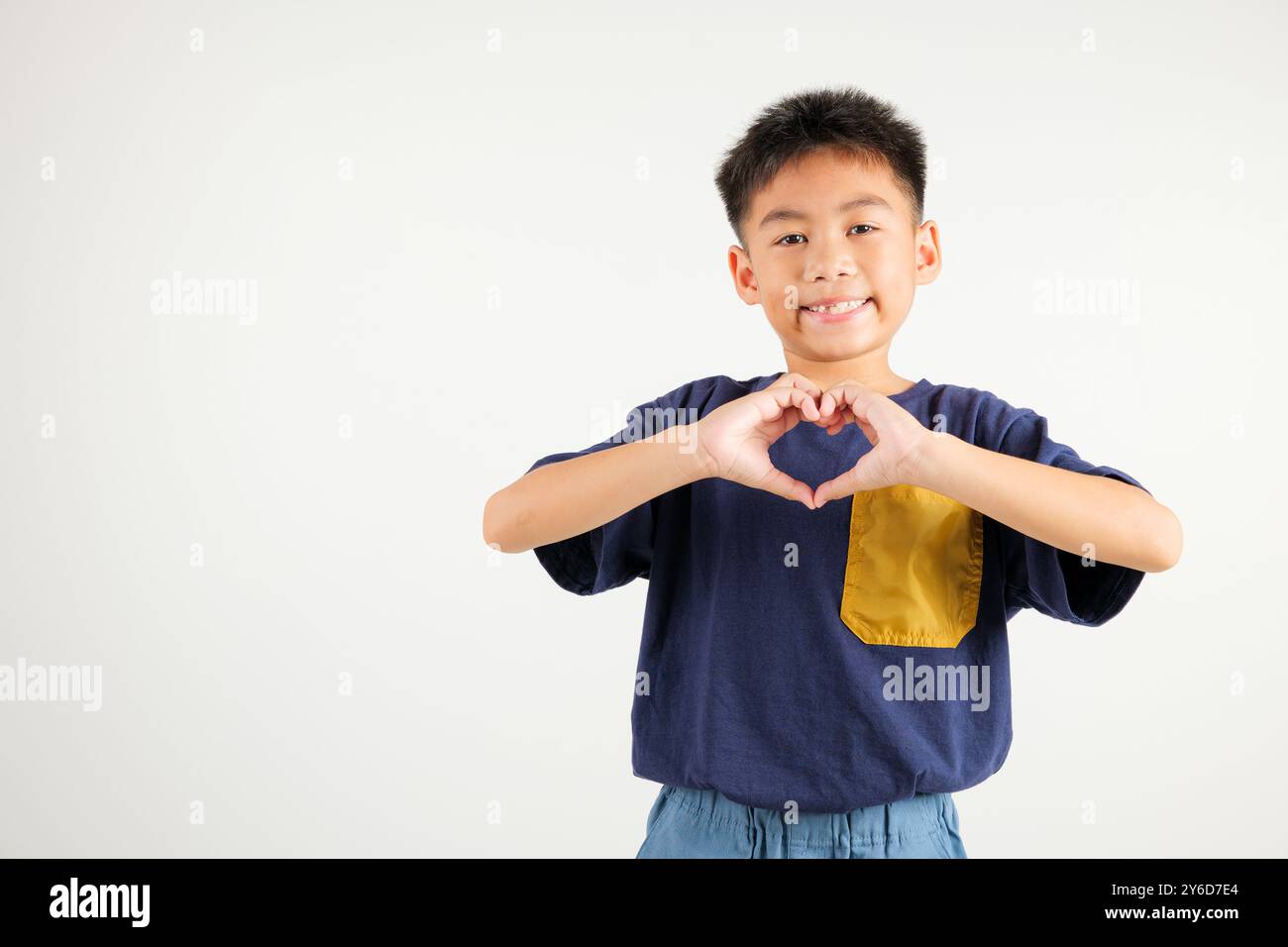 A smiling Asian young kid boy shows confidence, creating a heart shape ...