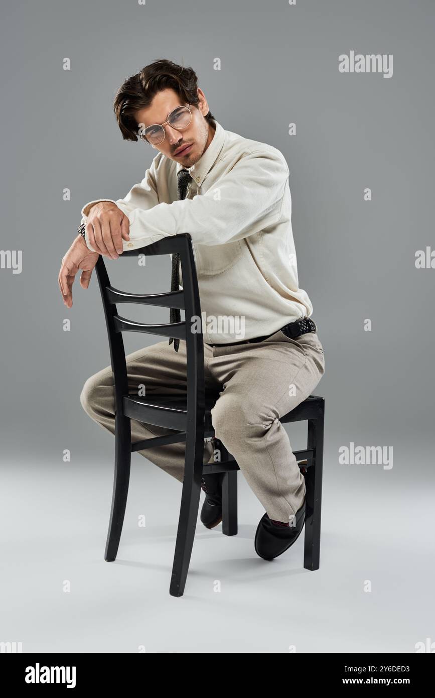 A young man dressed elegantly leans casually on a chair against a ...