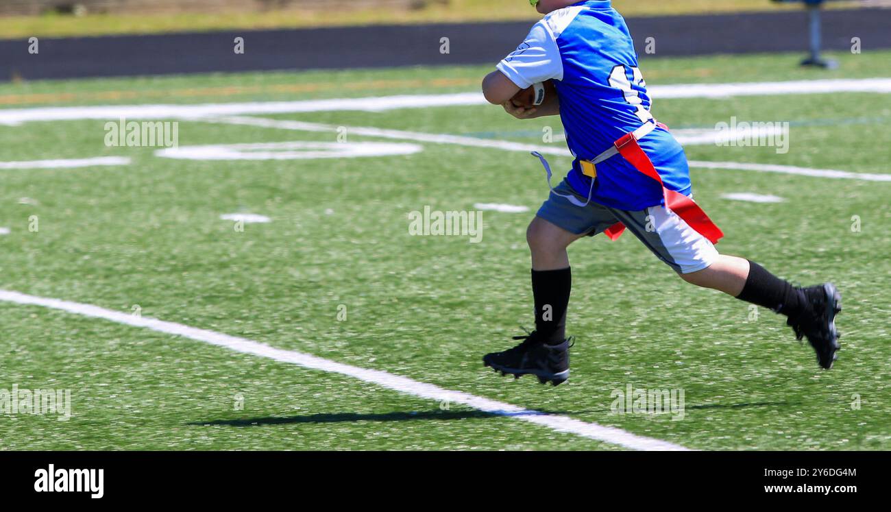 Flag football player running down the field holding the ball with two ...