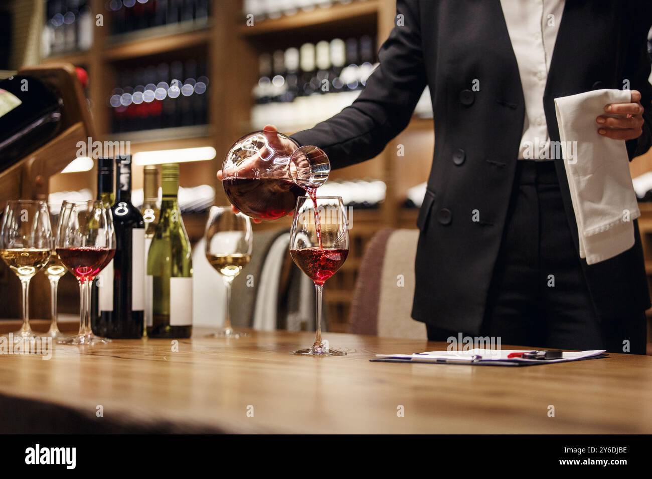 Woman bartender in strict classical clothes pouring red wine from ...
