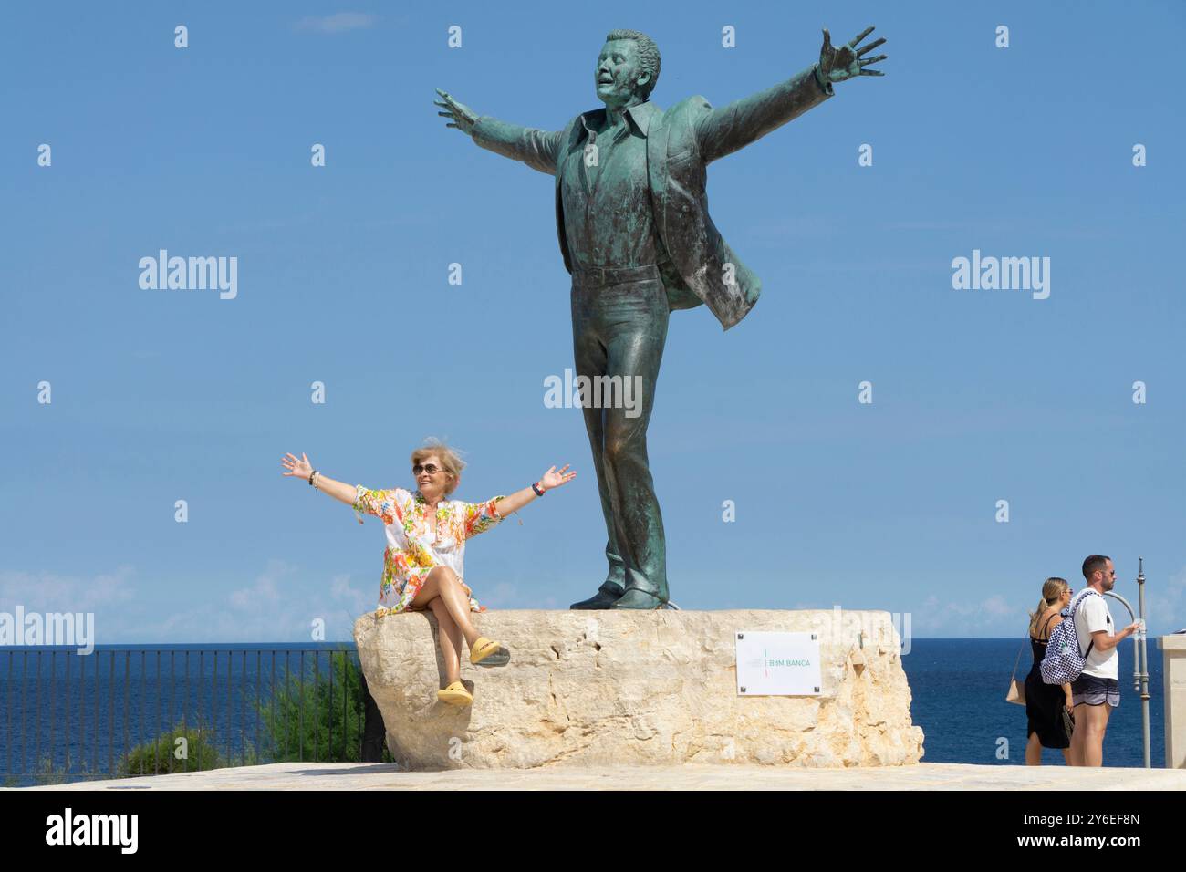 older woman sitting on plinth of statue bronze mimicing joyful pose ...