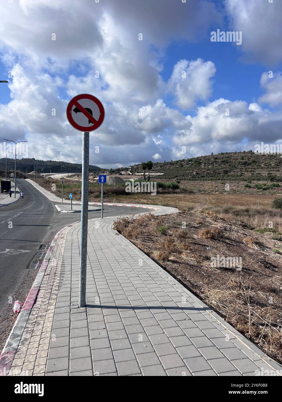 A No Left Turn road sign stands on a sidewalk along a rural road under ...