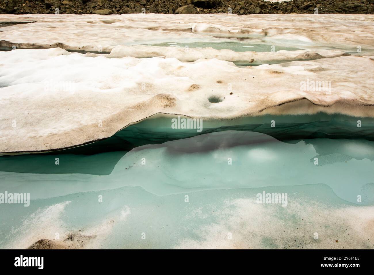 A partially melted glacier with turquoise ice and snow layers ...