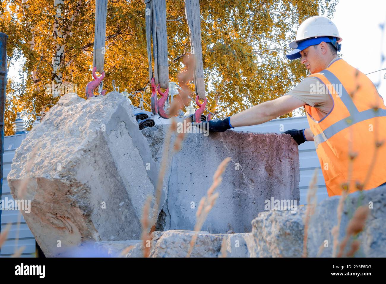 Construction worker in orange safety vest and hard hat adjusting slings ...