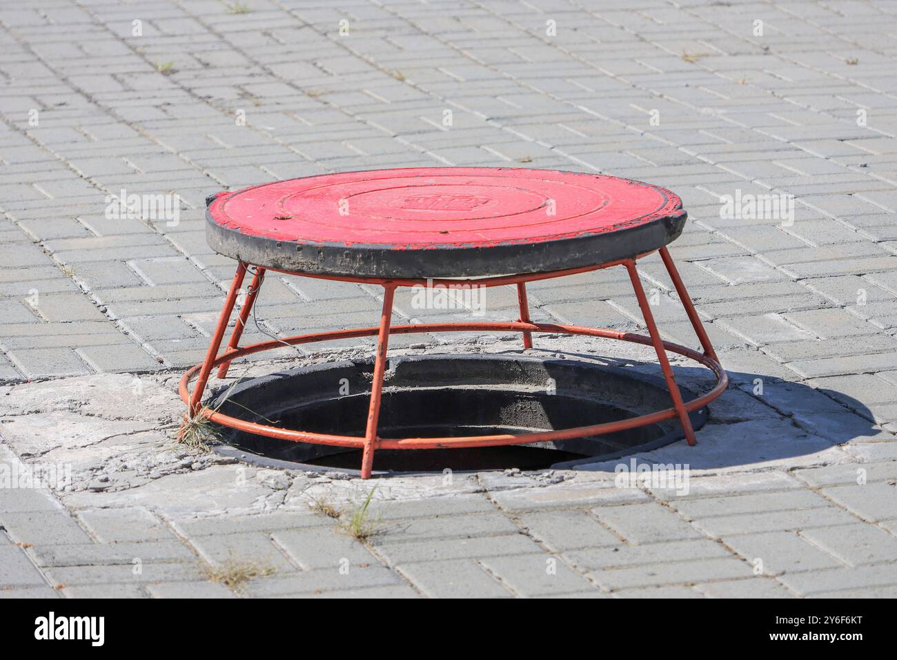 A red metal cover is placed over an open manhole surrounded by pavement ...