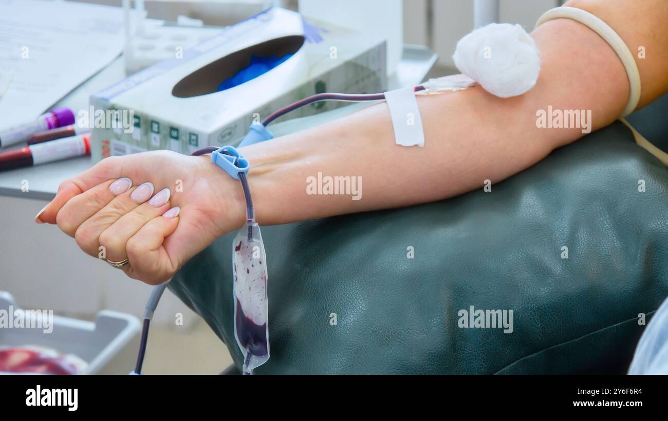 A person is shown donating blood, with a collection tube drawing blood ...