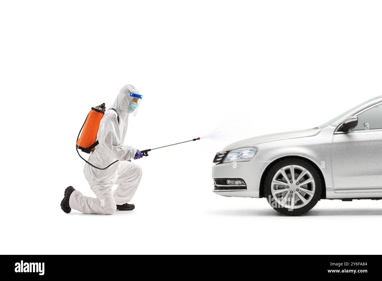 Man in a hazmat suit kneeling and disinfecting a car isolated on white ...