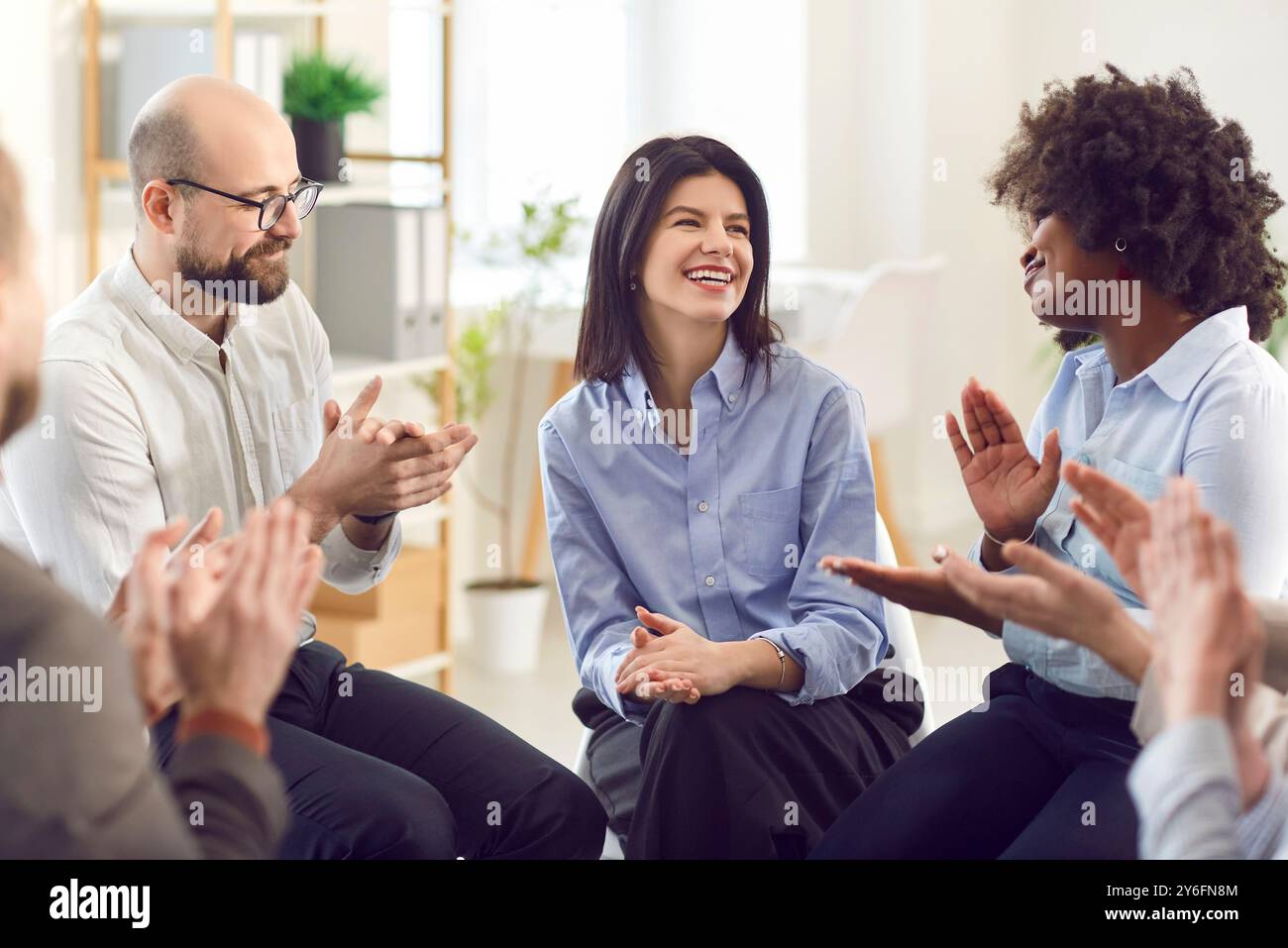 Group of coworkers sit in circle in office space and enthusiastically ...