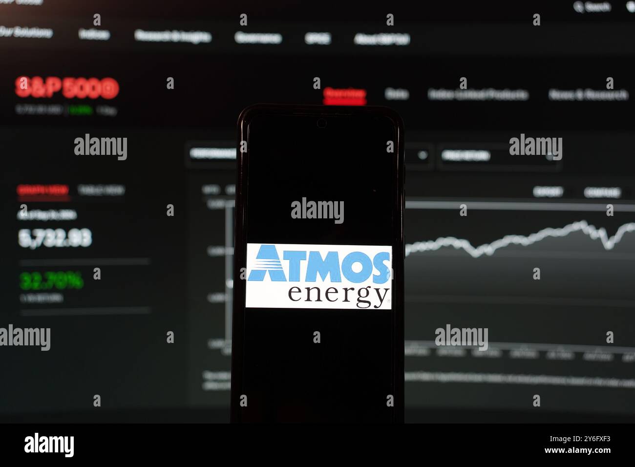 In this photo illustration, the Atmos Energy logo is displayed on a smartphone with a S&P index ...