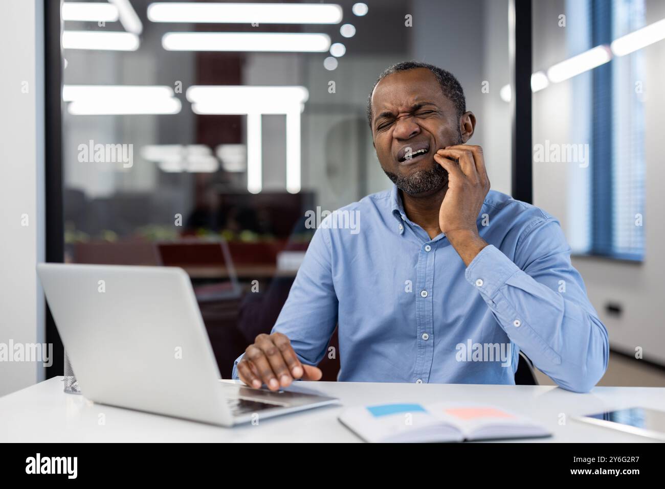 Man in office experiencing toothache, touching jaw in pain. Sits desk ...