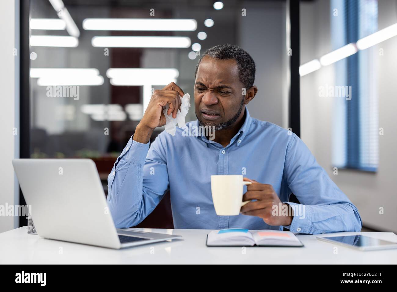 Office worker feeling unwell at desk, showing signs of illness. Holding ...