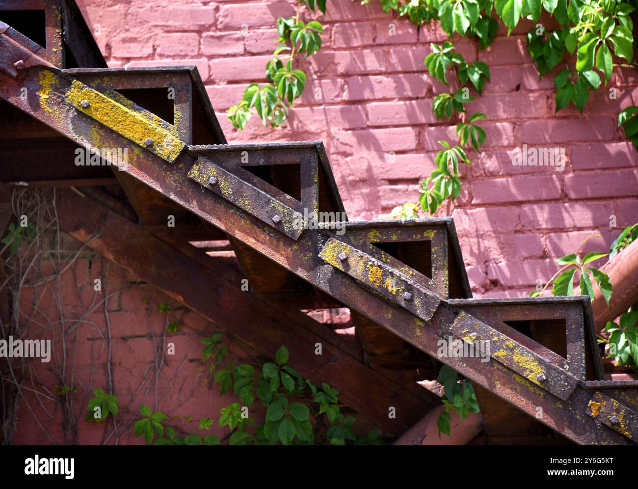 Metal, rusty stairs climb across a pink brick building. Stairs are ...