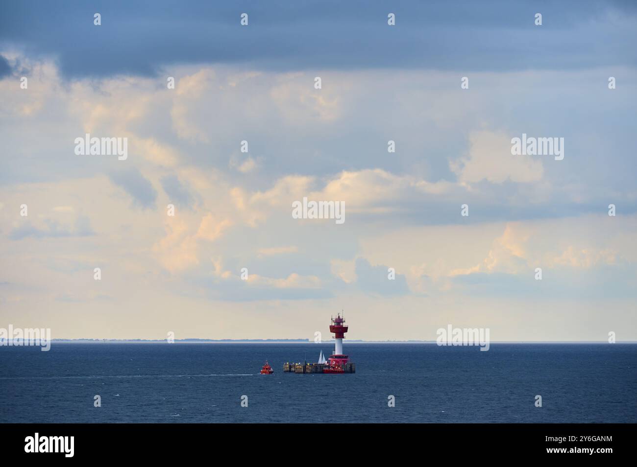 A red lighthouse stands on a calm, blue sea under a slightly cloudy sky ...