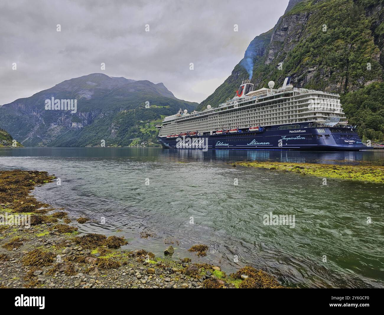 A large cruise ship, Mein Schiff 6, lies in the fjord, surrounded by ...