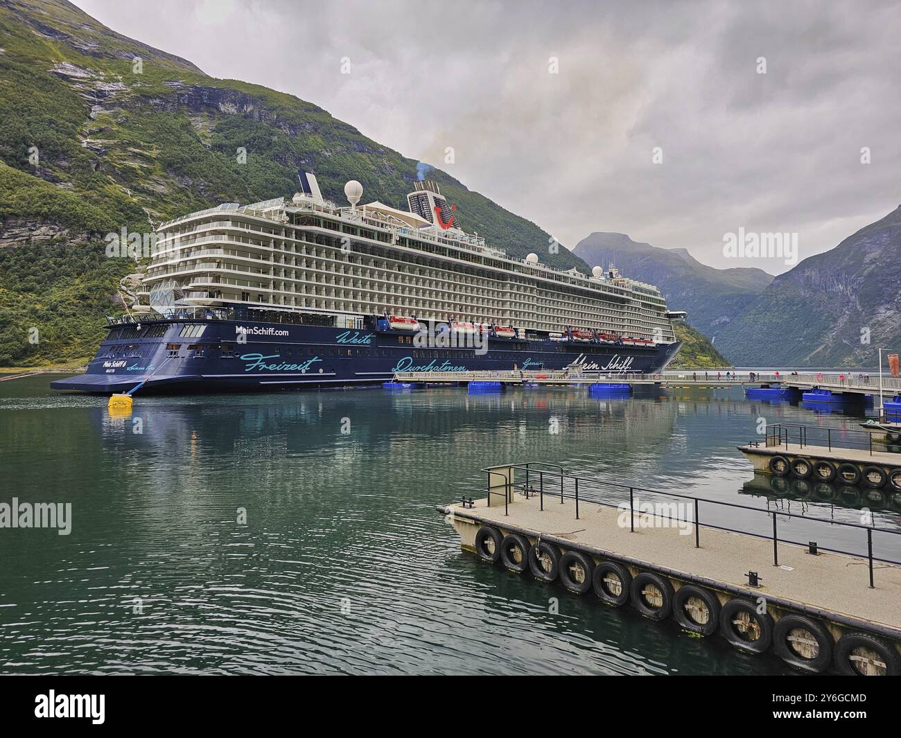 A large cruise ship, Mein Schiff 6, lies in the fjord, surrounded by ...