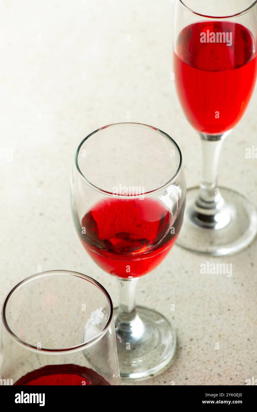 Three wine glasses filled with red syrup form a diagonal line on the ...