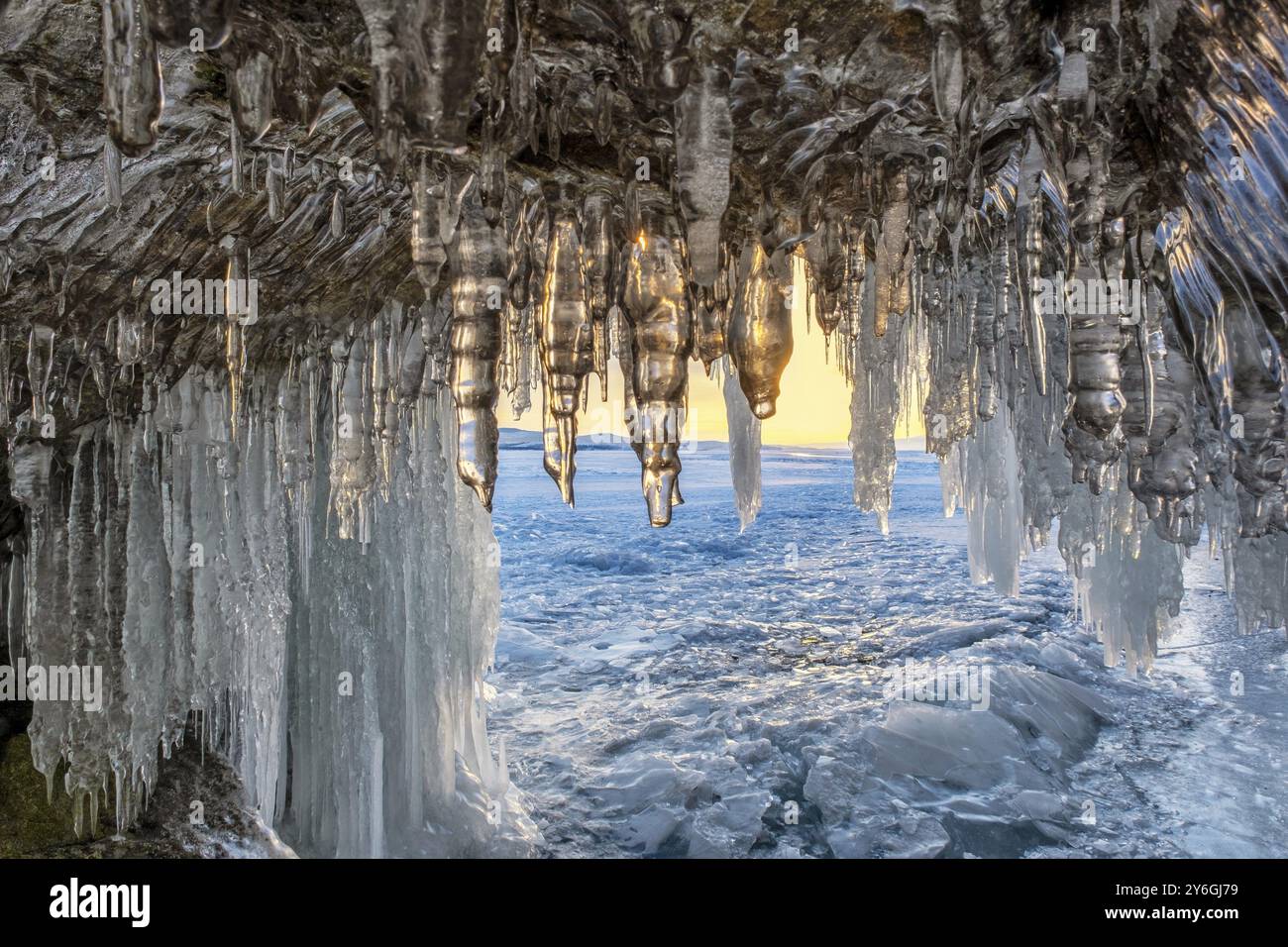 Ice cave on Baikal lake in winter. Blue ice and icicles in grotto in the sunset sunlight. Olkhon ...