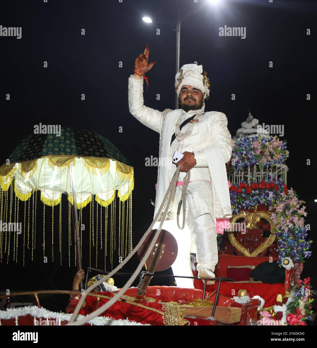 A groom in traditional attire stands on a decorated carriage during a ...
