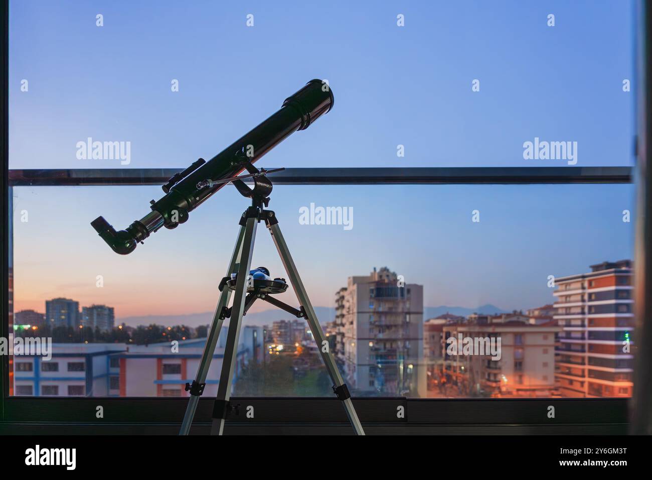 Telescope on tripod standing inside against city and sky background ...