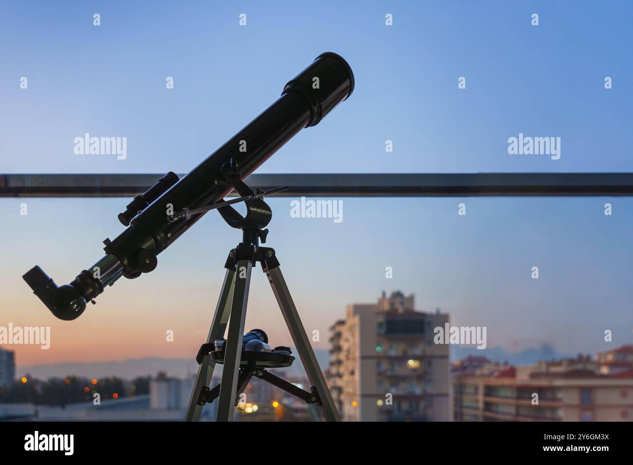 A telescope stands ready near a window, pointed at the twilight sky ...
