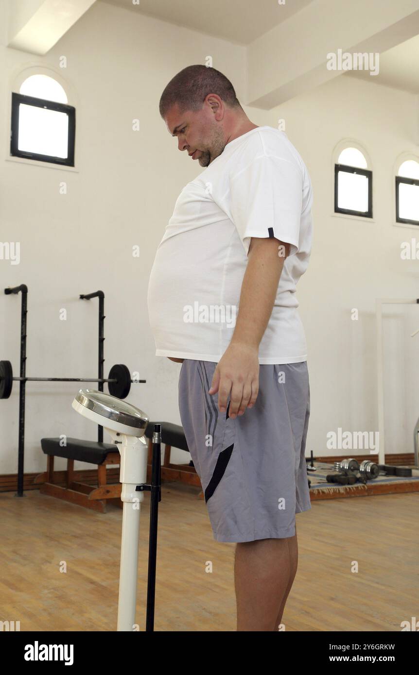 Man with overweight standing on scales in the gym Stock Photo - Alamy