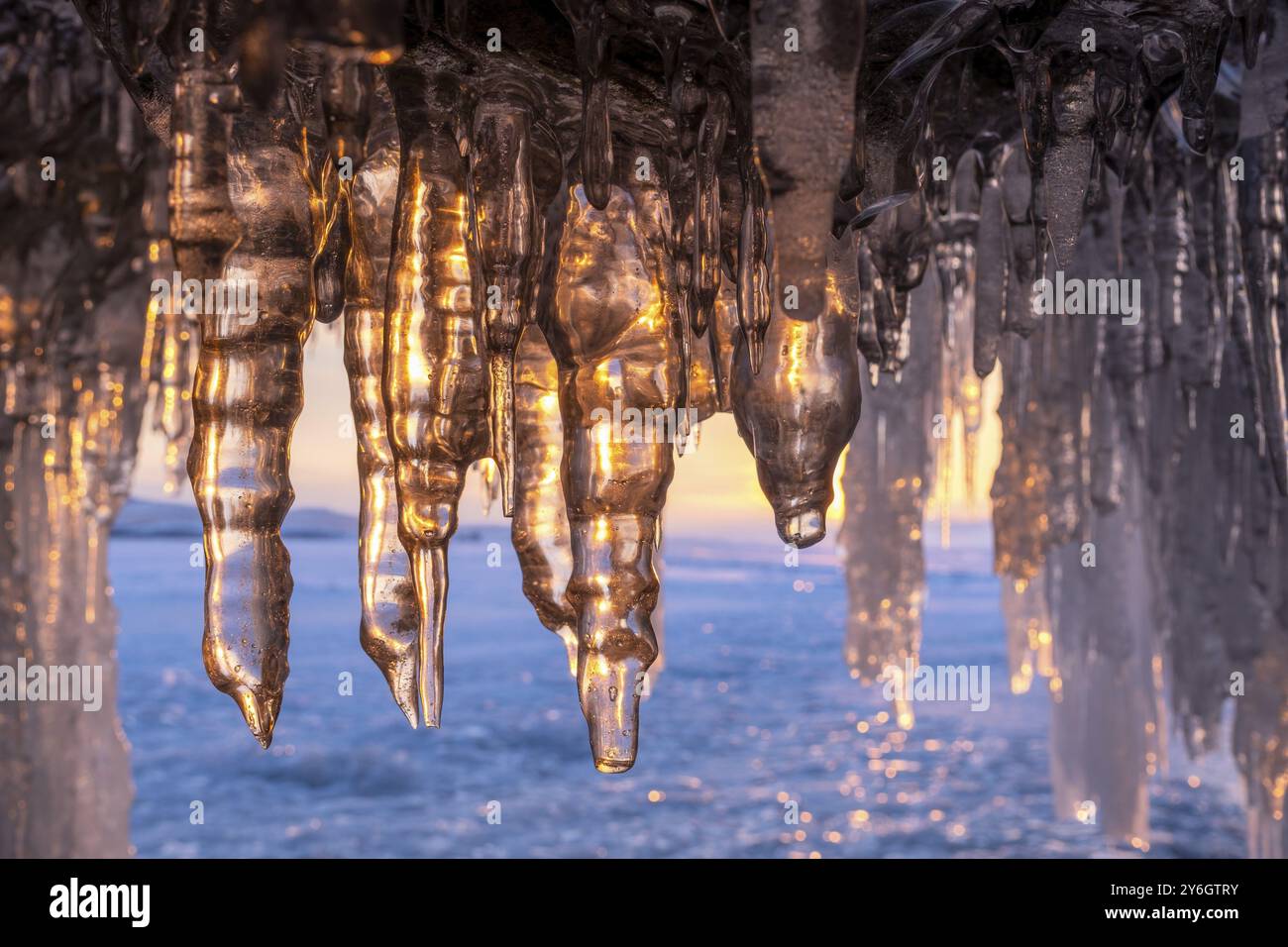 Ice cave on Baikal lake in winter. Blue ice and icicles in grotto in the sunset sunlight. Olkhon ...