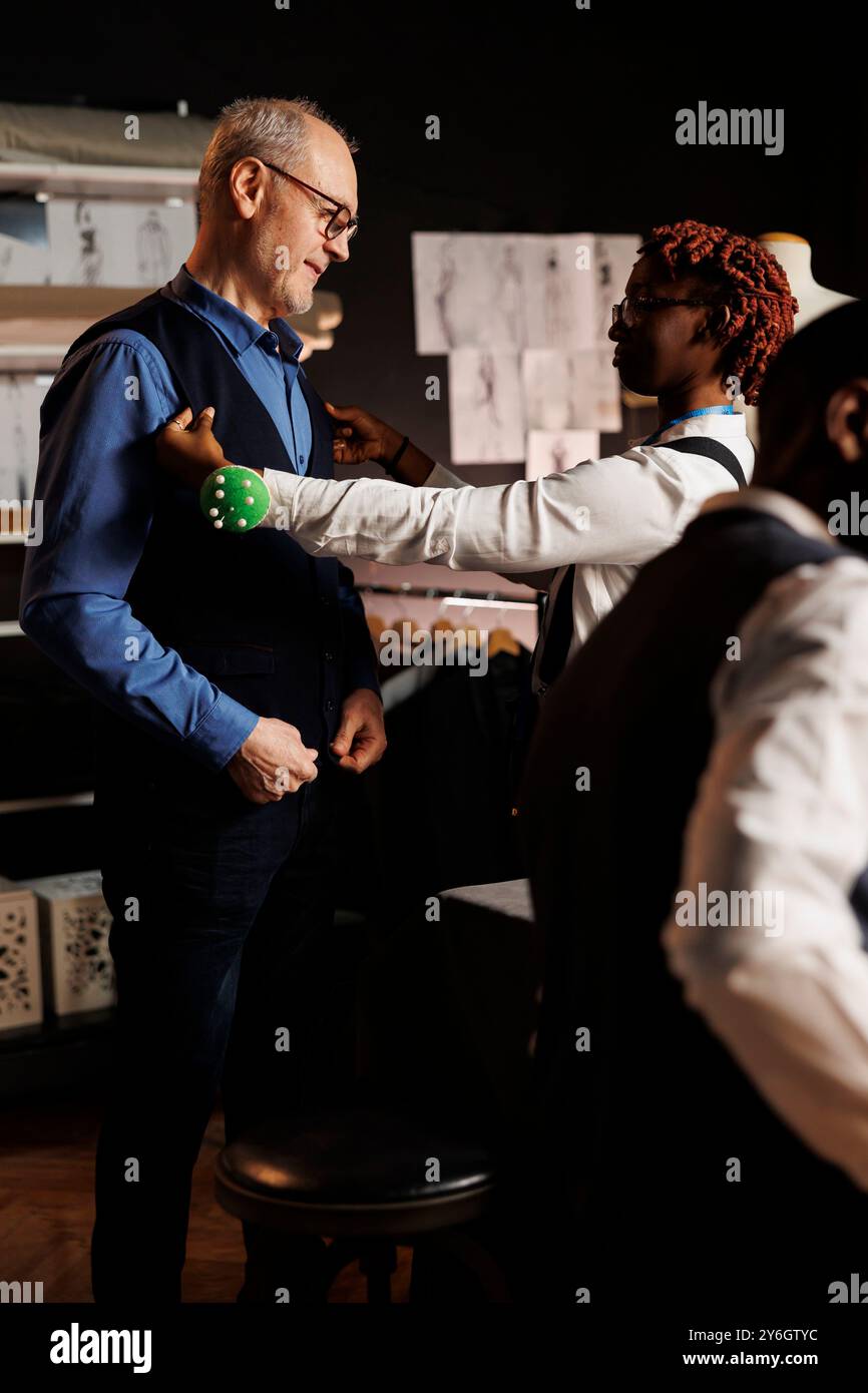 Masterful seamstress helping elderly customer try on custom made ...