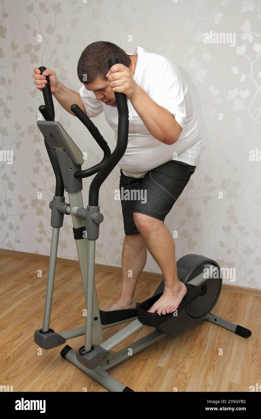 Overweight man exercising on trainer ellipsoid Stock Photo - Alamy
