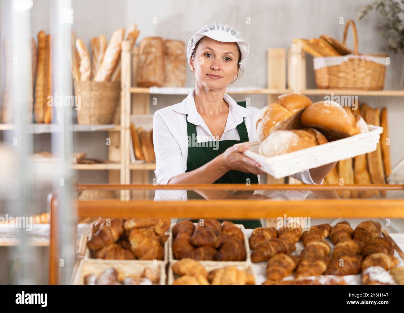 Positive female bakery employee offering bread and different baguettes ...