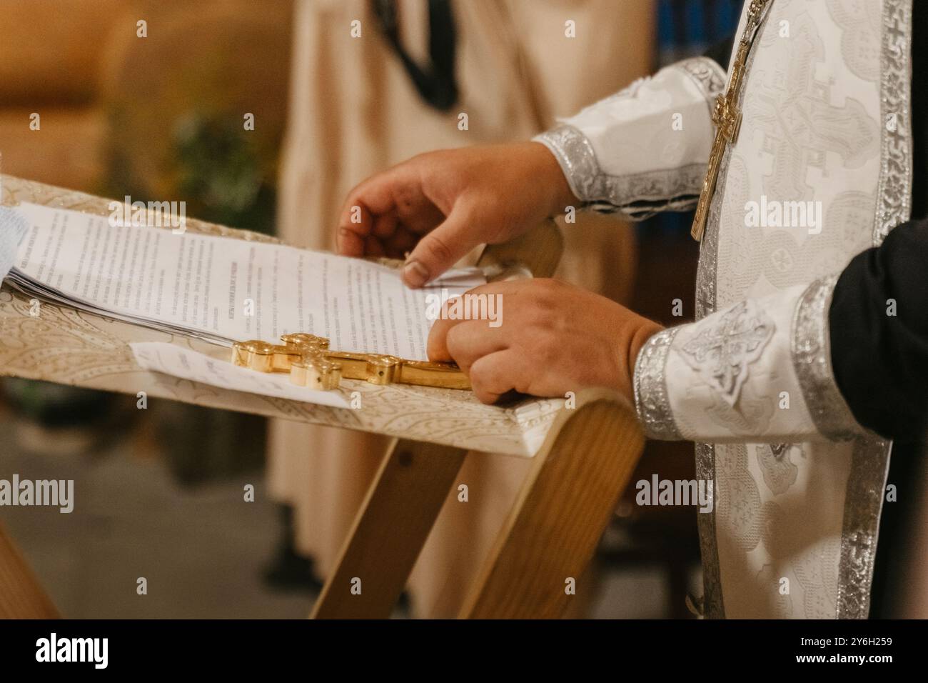 A priest in a white robe reads from a scriptural text during a baptism ceremony in a church ...