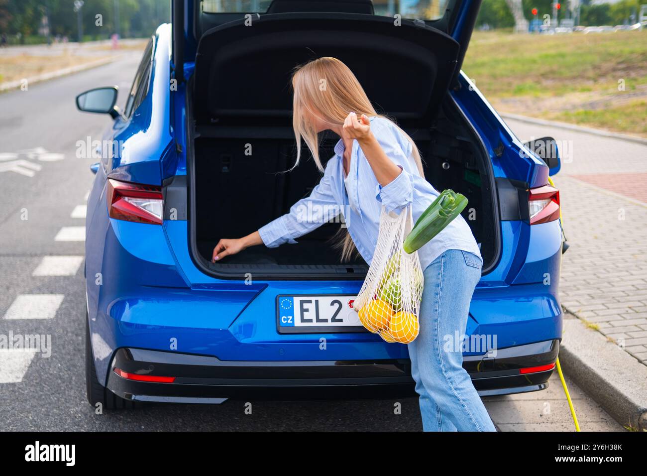 Young woman unloading groceries from the trunk of a blue electric car ...