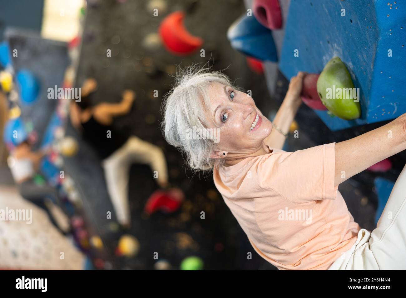 Mature female fitness climber training at bouldering gym.Woman rise up ...