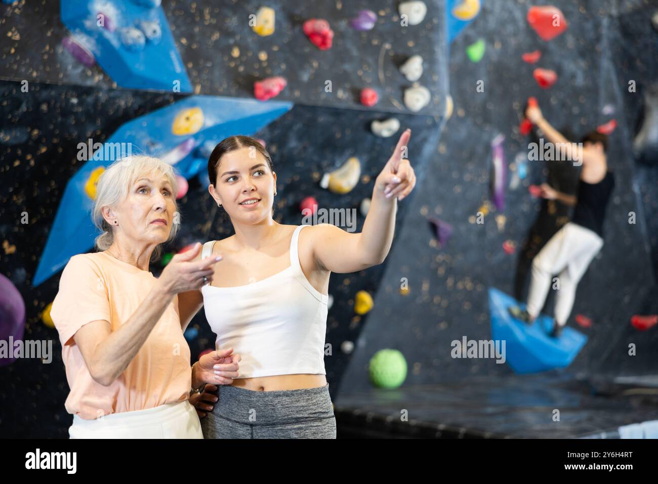 Young female climbing instructor explaining wall climbing to mature ...