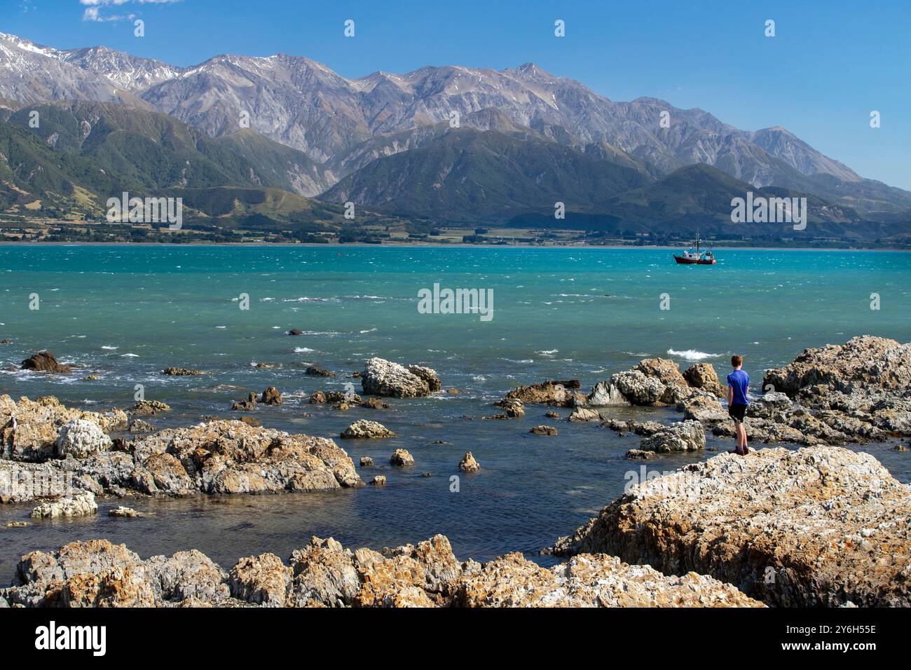Charlie standing on rocks with the Seaward Kaikoura Range mountains in ...