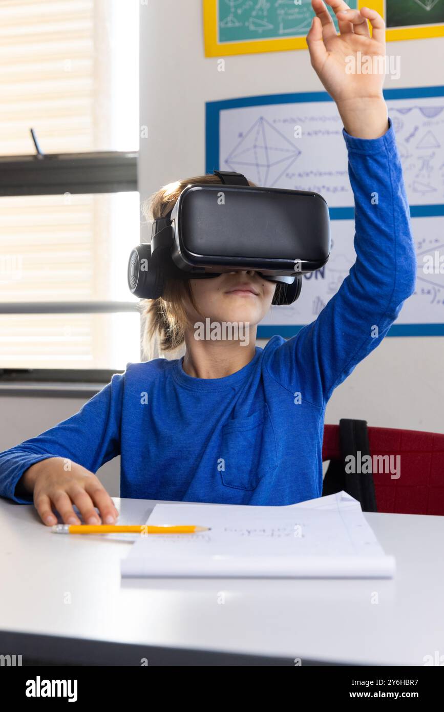 Using VR headset, boy raising hand in classroom, engaging in school ...