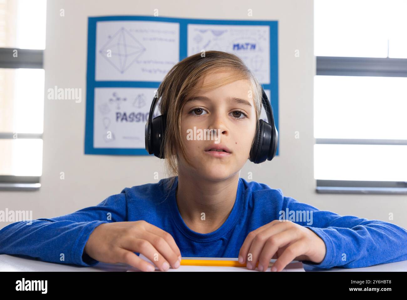 In school, boy wearing headphones and holding pencil, focusing on ...