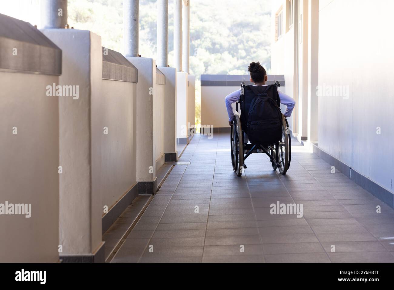 In school, student in wheelchair moving through hallway, carrying ...