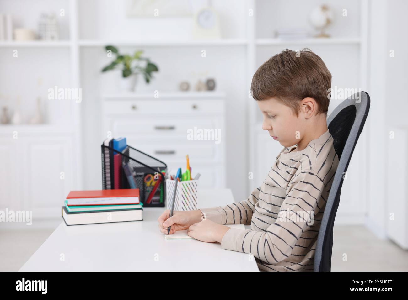 Boy with correct posture doing homework at white desk indoors Stock ...