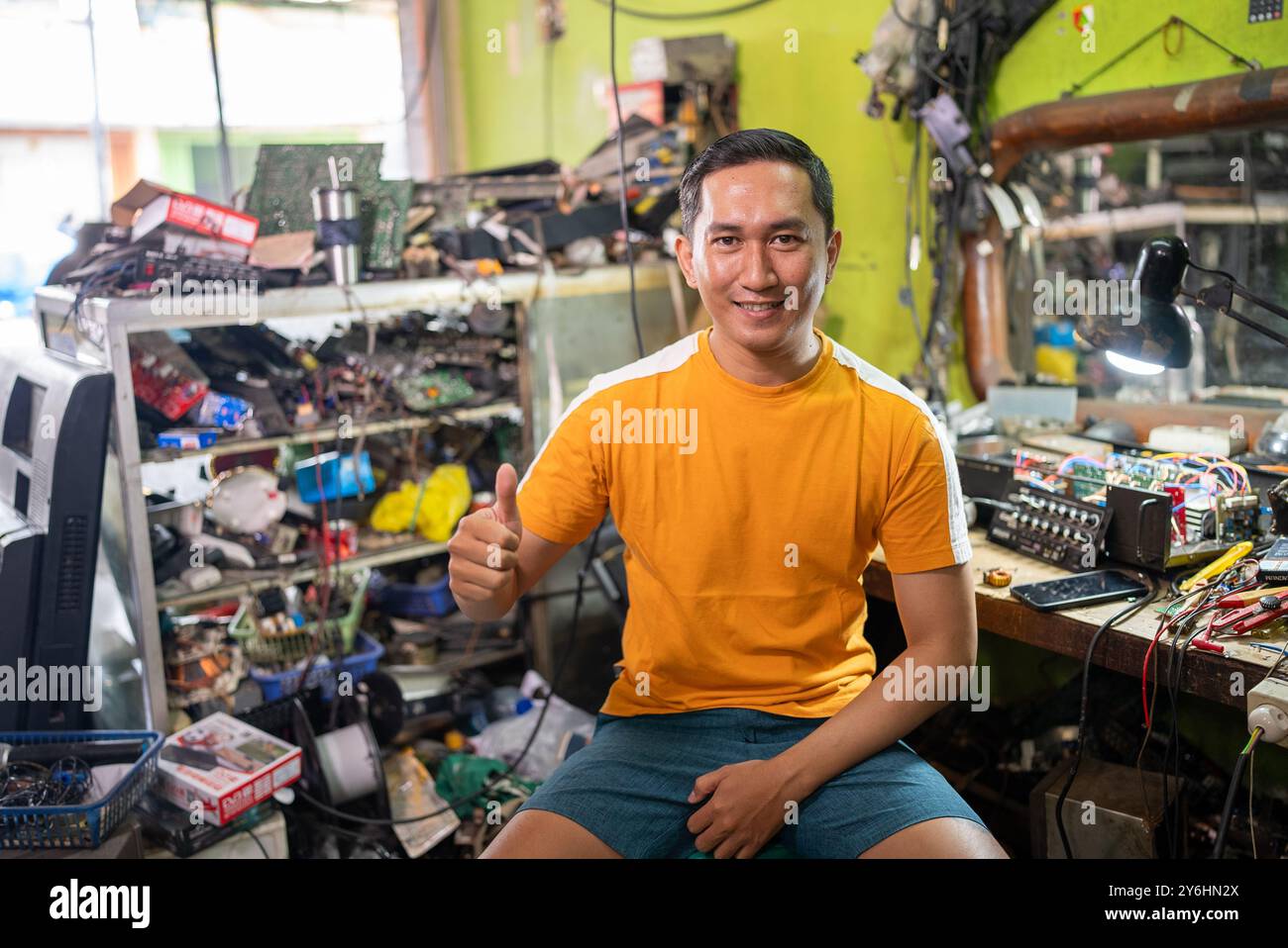 male electronics repairman sits showing thumbs up at an service station ...