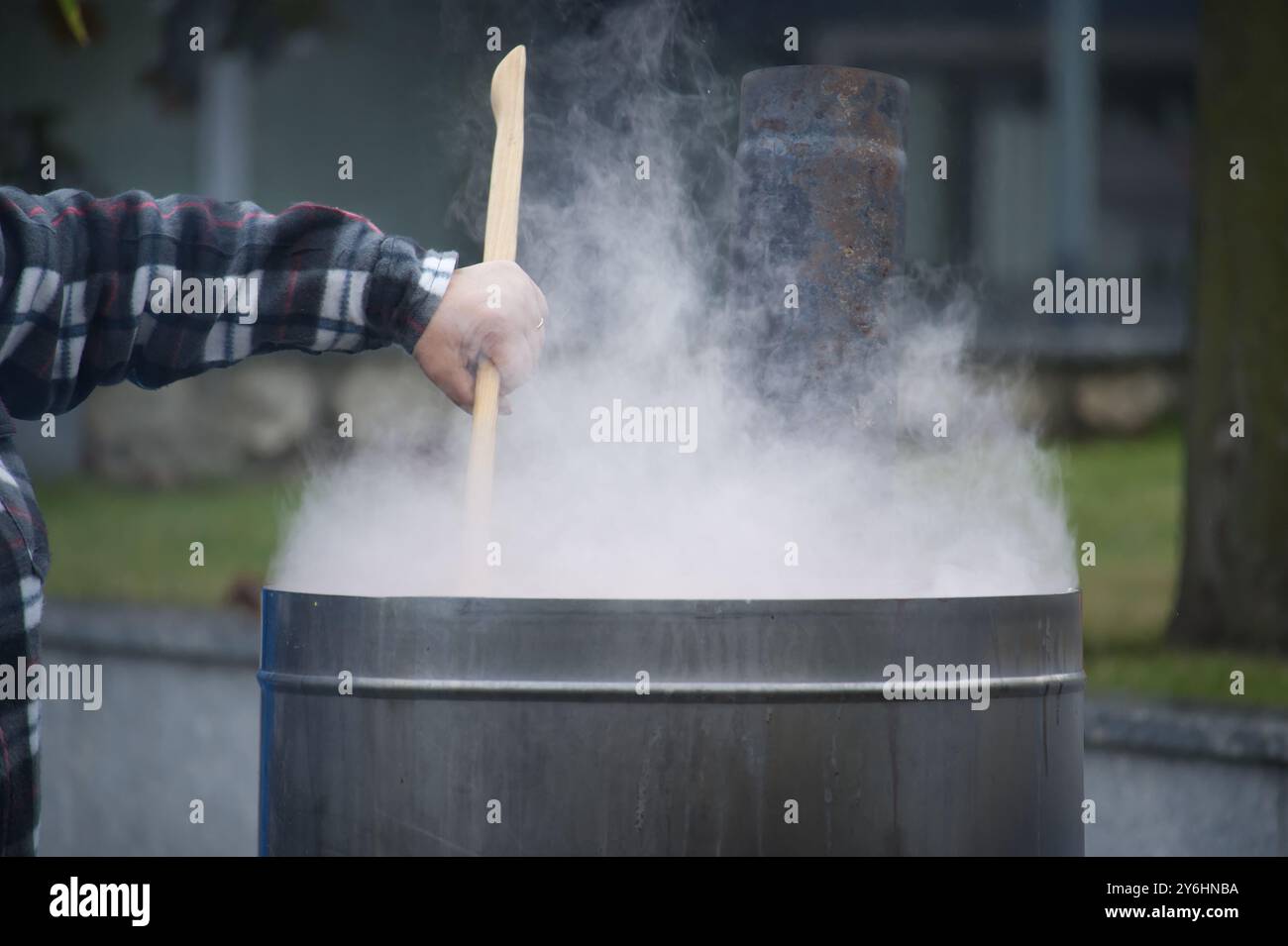 A person stirring a large pot with steam rising, indicating cooking or ...