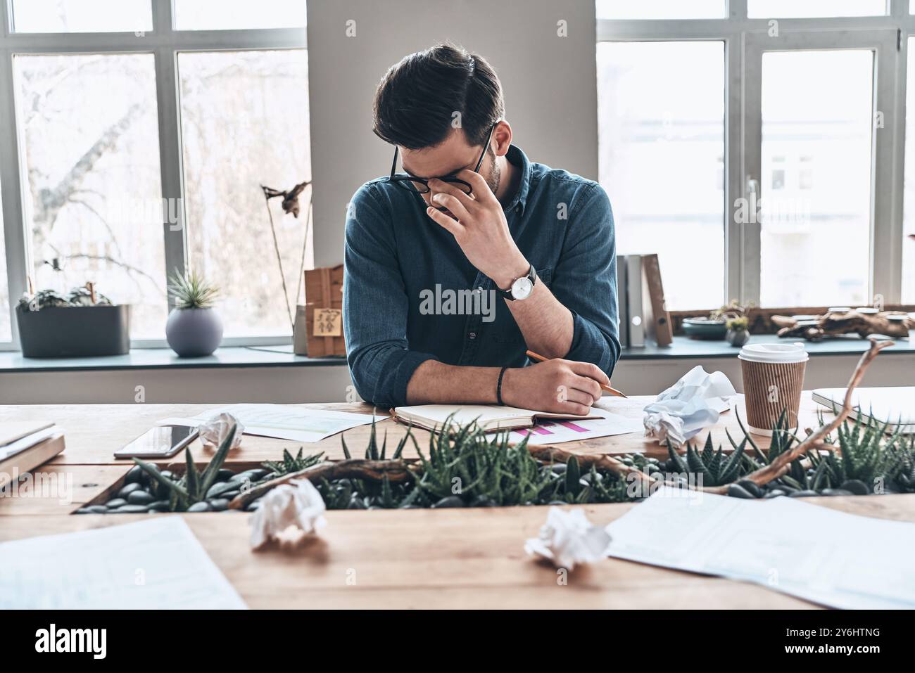 Overworked. Tired young man writing something down in personal ...