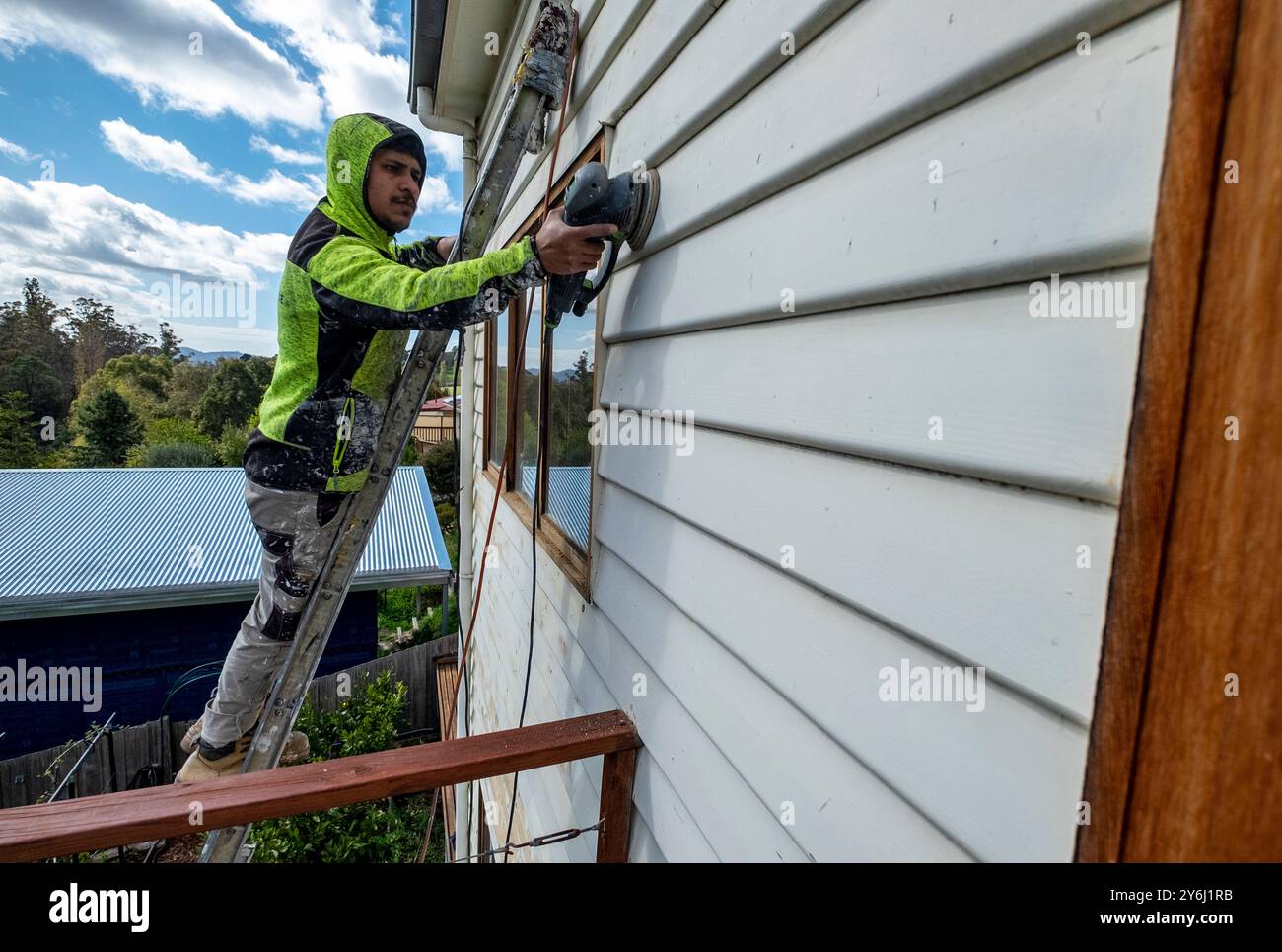 Painter on ladder doing surface preparation on a timber weatherboard ...