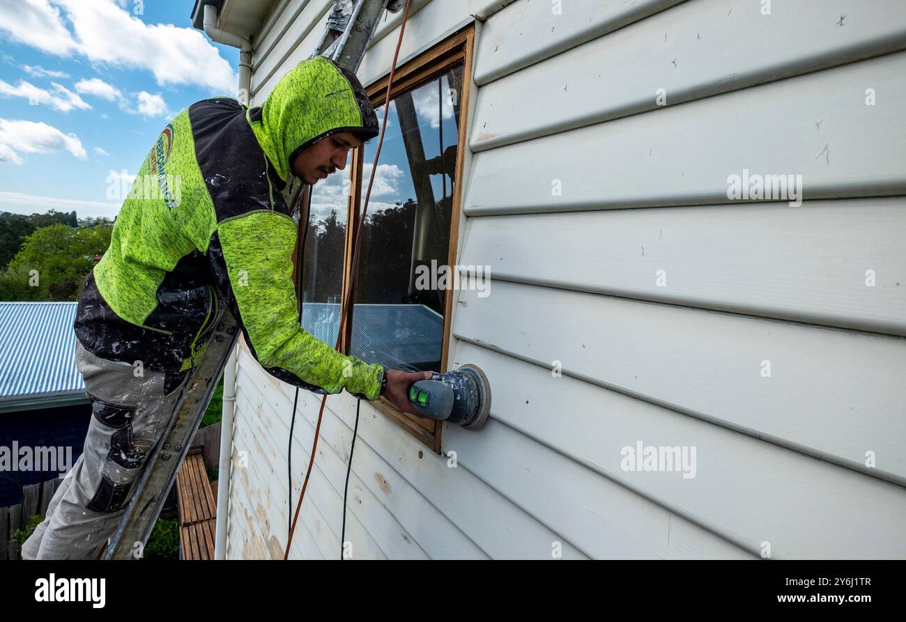Painter on ladder doing surface preparation on a timber weatherboard ...