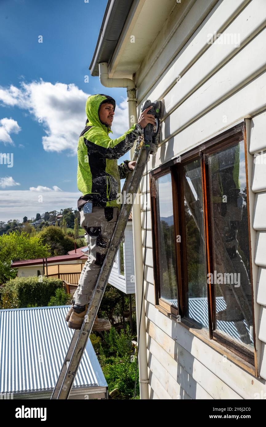 Painter on ladder doing surface preparation on a timber weatherboard ...