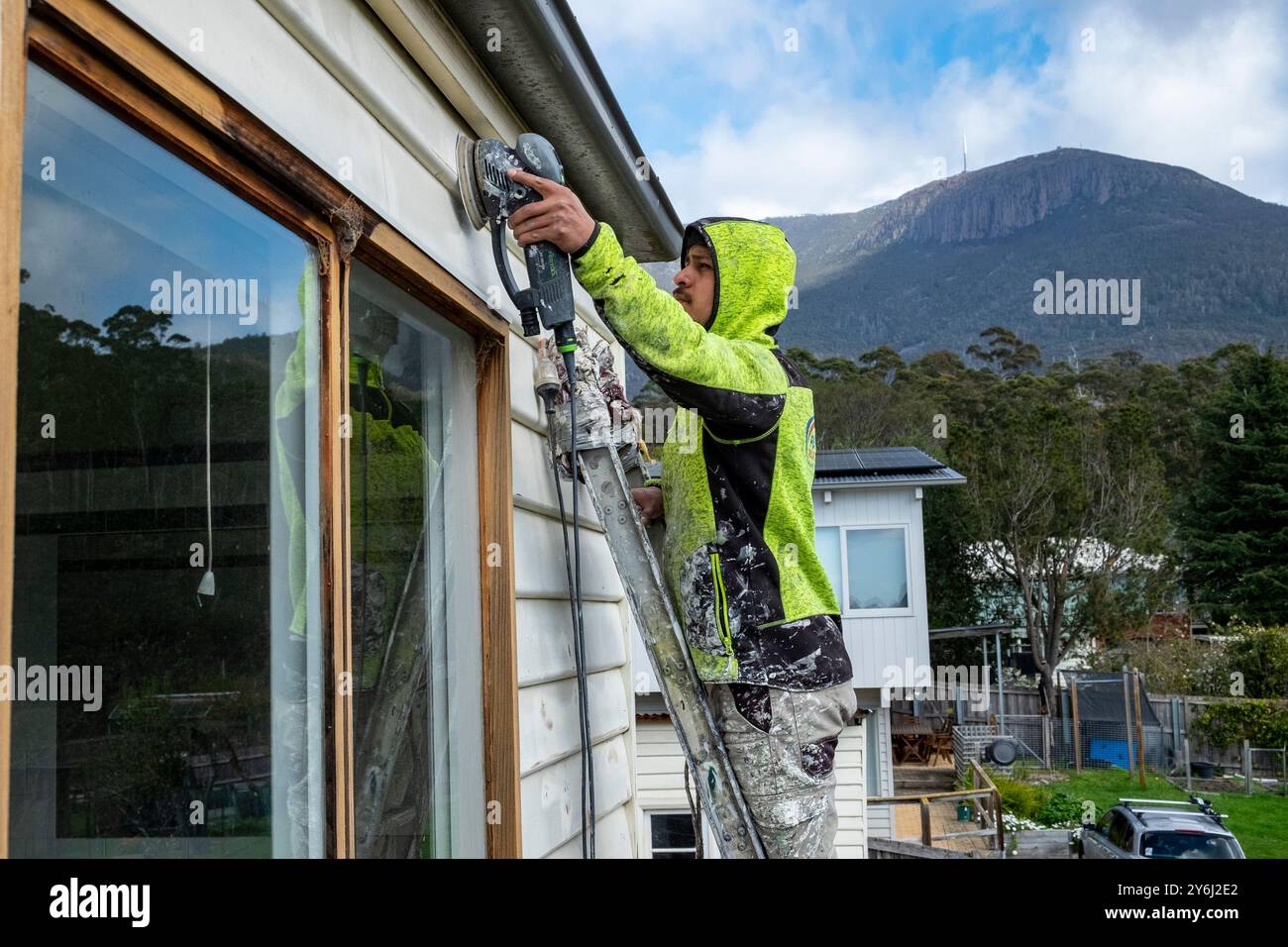 Painter on ladder doing surface preparation on a timber weatherboard ...